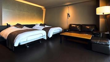 Quarto de hotel com duas camas, um sofá, uma mesa de centro e uma luminária.