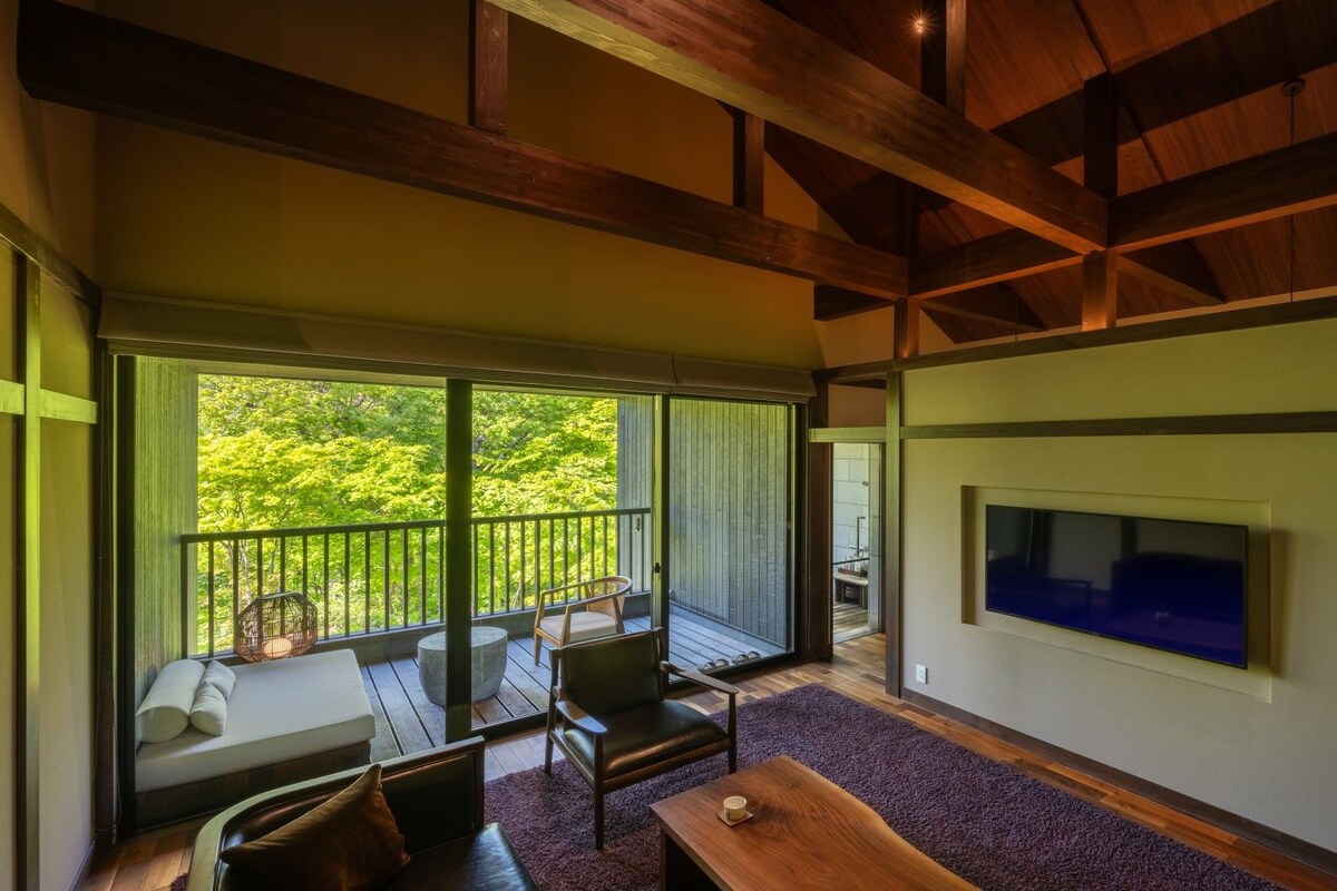 Quarto amplo com uma grande janela, uma TV de tela plana na parede e teto de madeira.