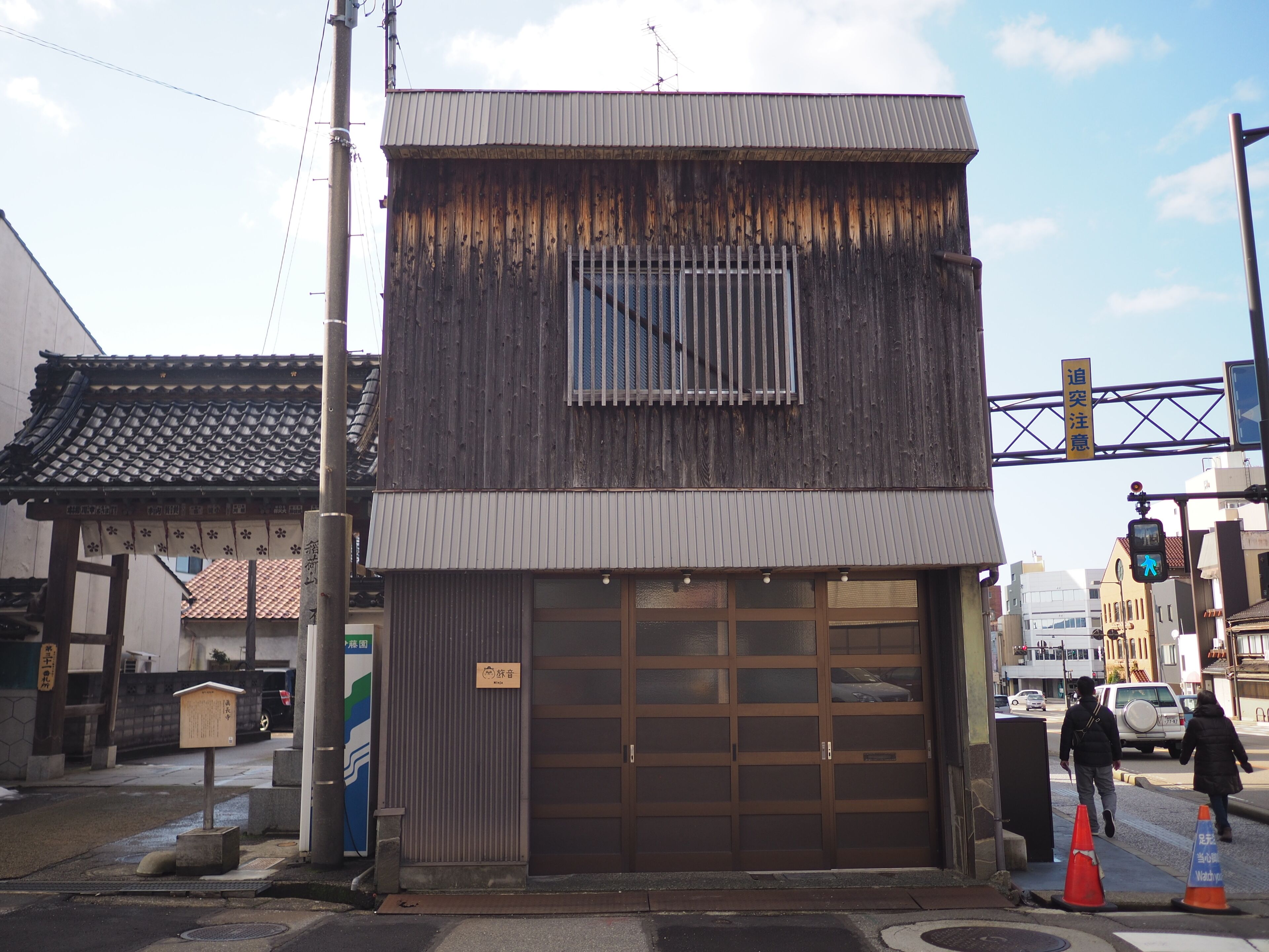 Um edifício com telhado de azulejos tradicionais, uma porta de garagem grande e uma placa com caracteres japoneses.