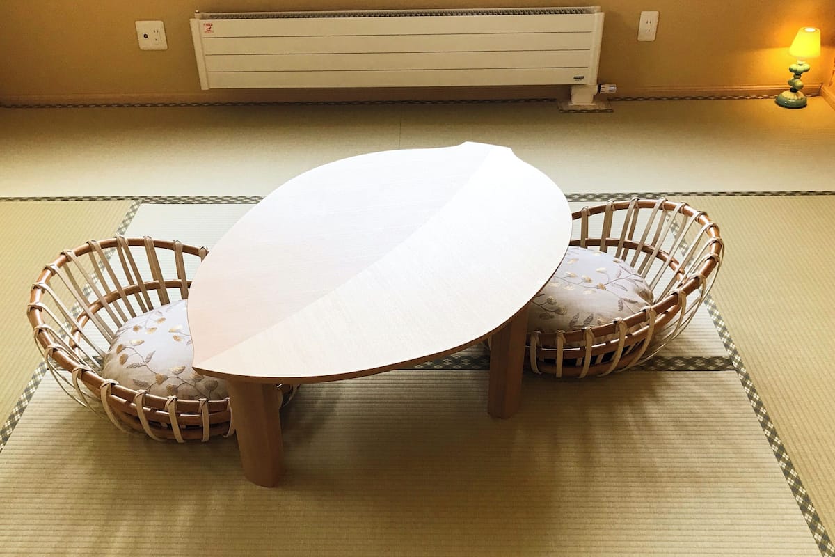 Um espaço com esteiras de tatame, uma mesa baixa e duas cadeiras de palha.