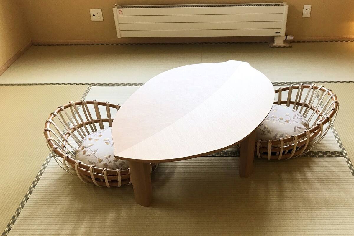 Um espaço com esteiras de tatame, uma mesa baixa e duas cadeiras de fibra.