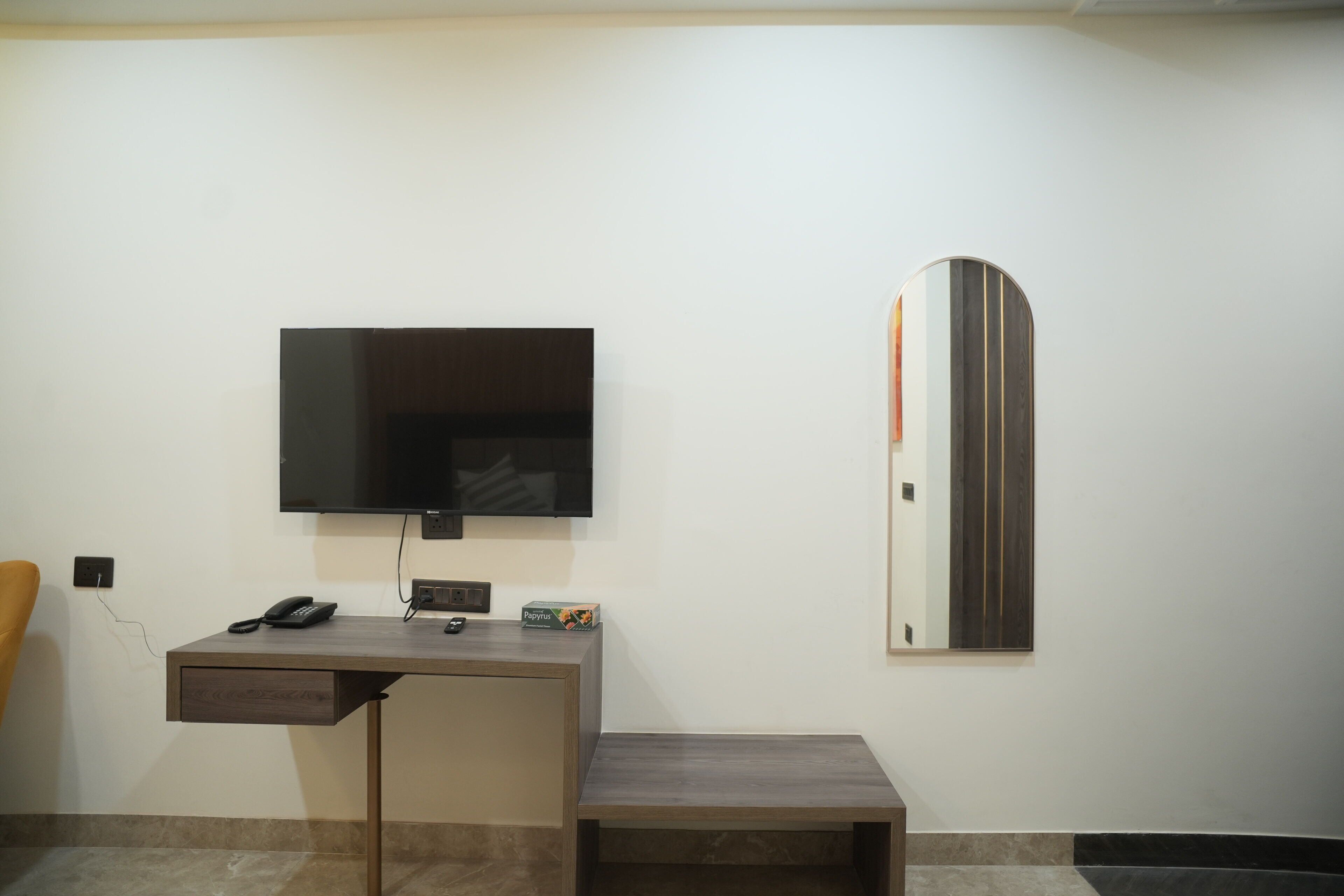 Quarto moderno com televisão de tela plana na parede, uma mesa com telefone e um pequeno banco.