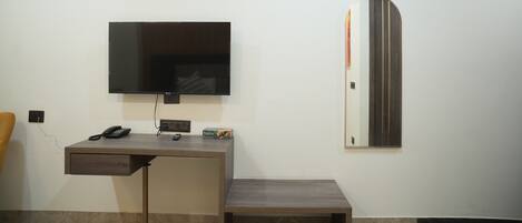 Quarto moderno com televisão de tela plana na parede, uma mesa com telefone e um pequeno banco.