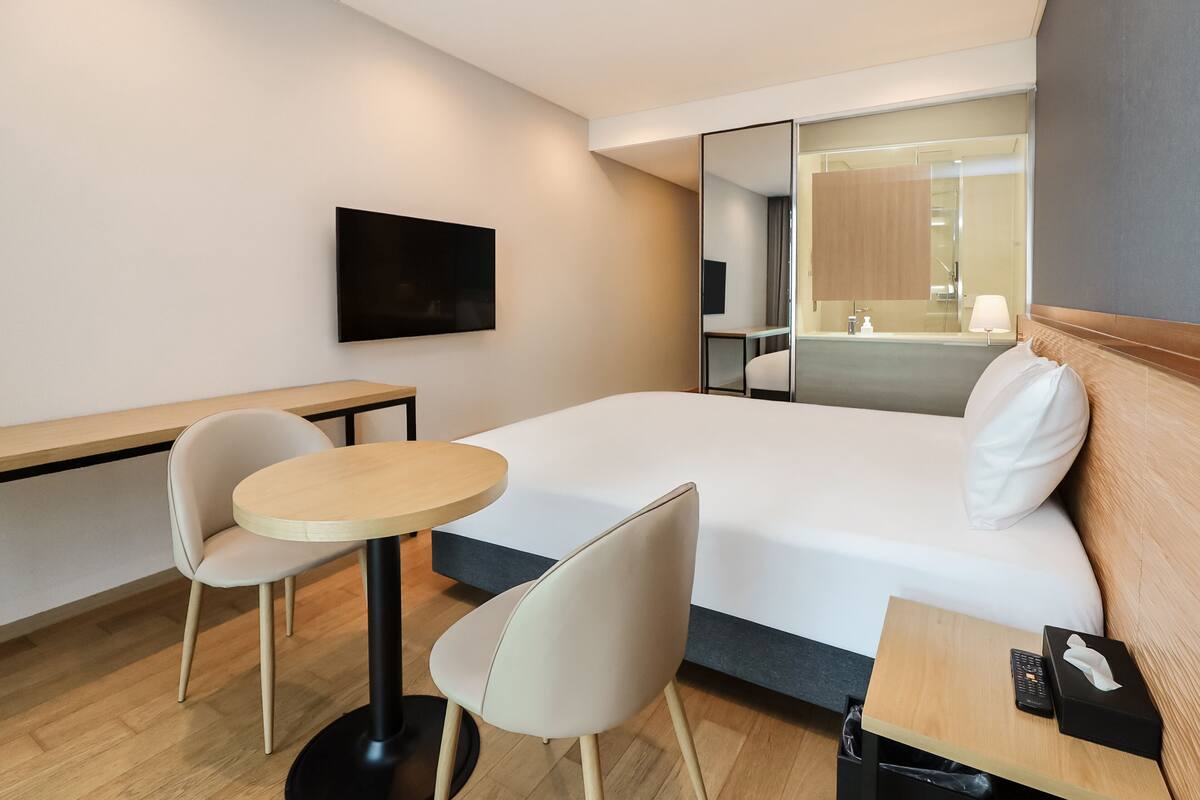 Quarto de hotel moderno com cama, escrivaninha, cadeira, televisão e espelho.