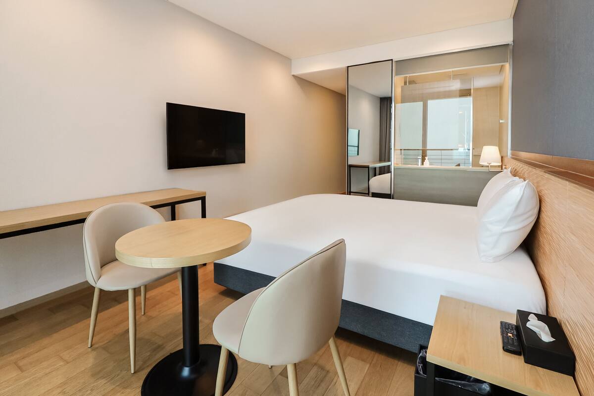Quarto de hotel com uma cama, uma escrivaninha, uma cadeira, uma televisão e um espelho.