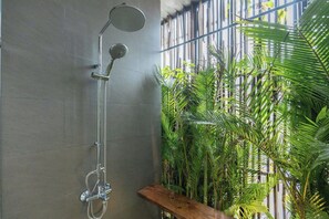 Chuveiro com chuveiro de teto e mangueira, um banco de madeira e uma parede coberta de plantas verdes.