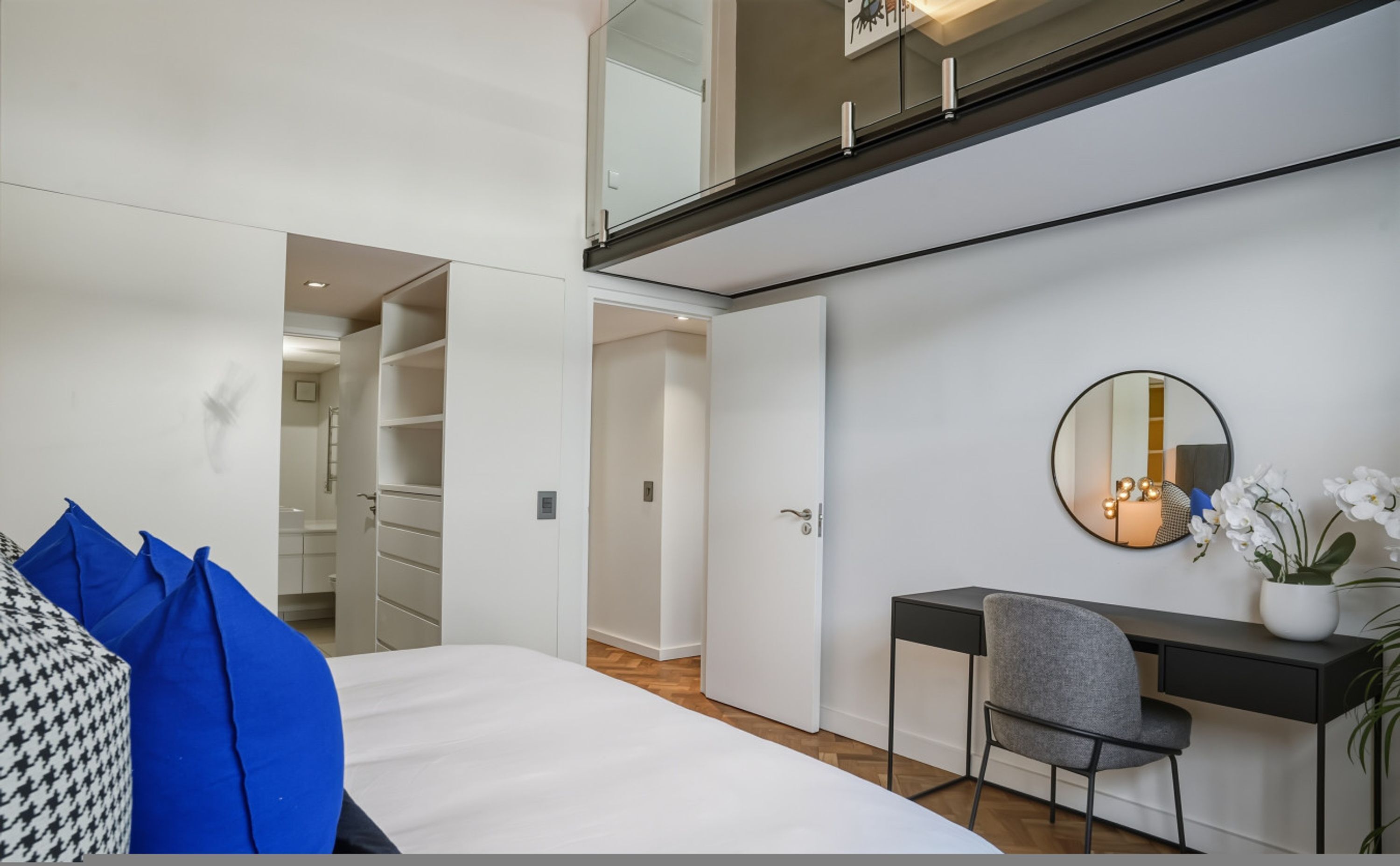 Quarto moderno com cama, escrivaninha e cadeira. Há um guarda-roupa com espelho e uma planta na escrivaninha.