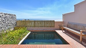 Piscina no terraço com um banco de madeira e uma parede de pedra.