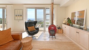 Uma sala de estar ampla com um sofá de couro preto, uma lareira a lenha vermelha e vista para o exterior através de grandes portas de correr.
