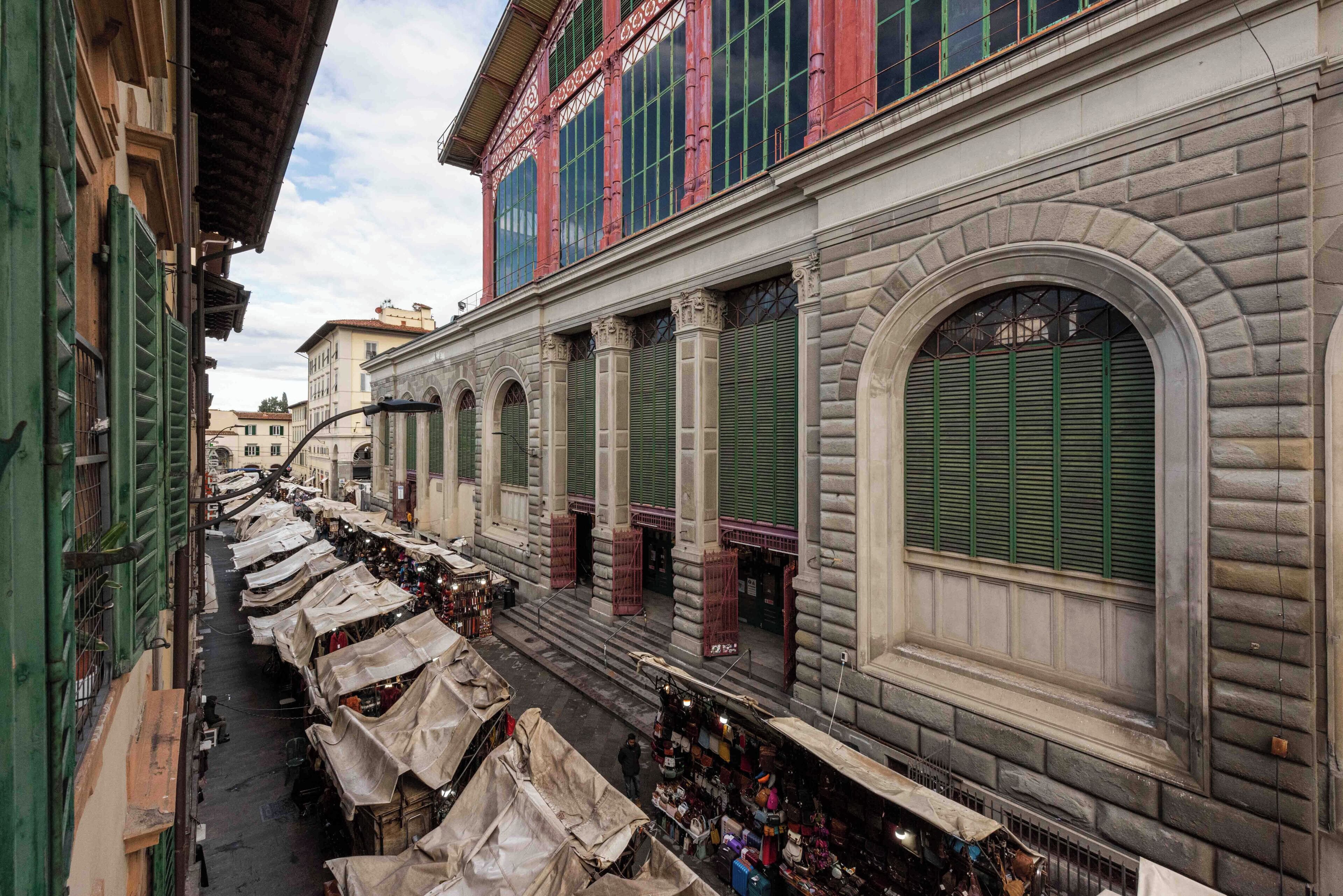 Ruas com bancas de mercado e um edifício histórico com janelas em arco e persianas verdes.