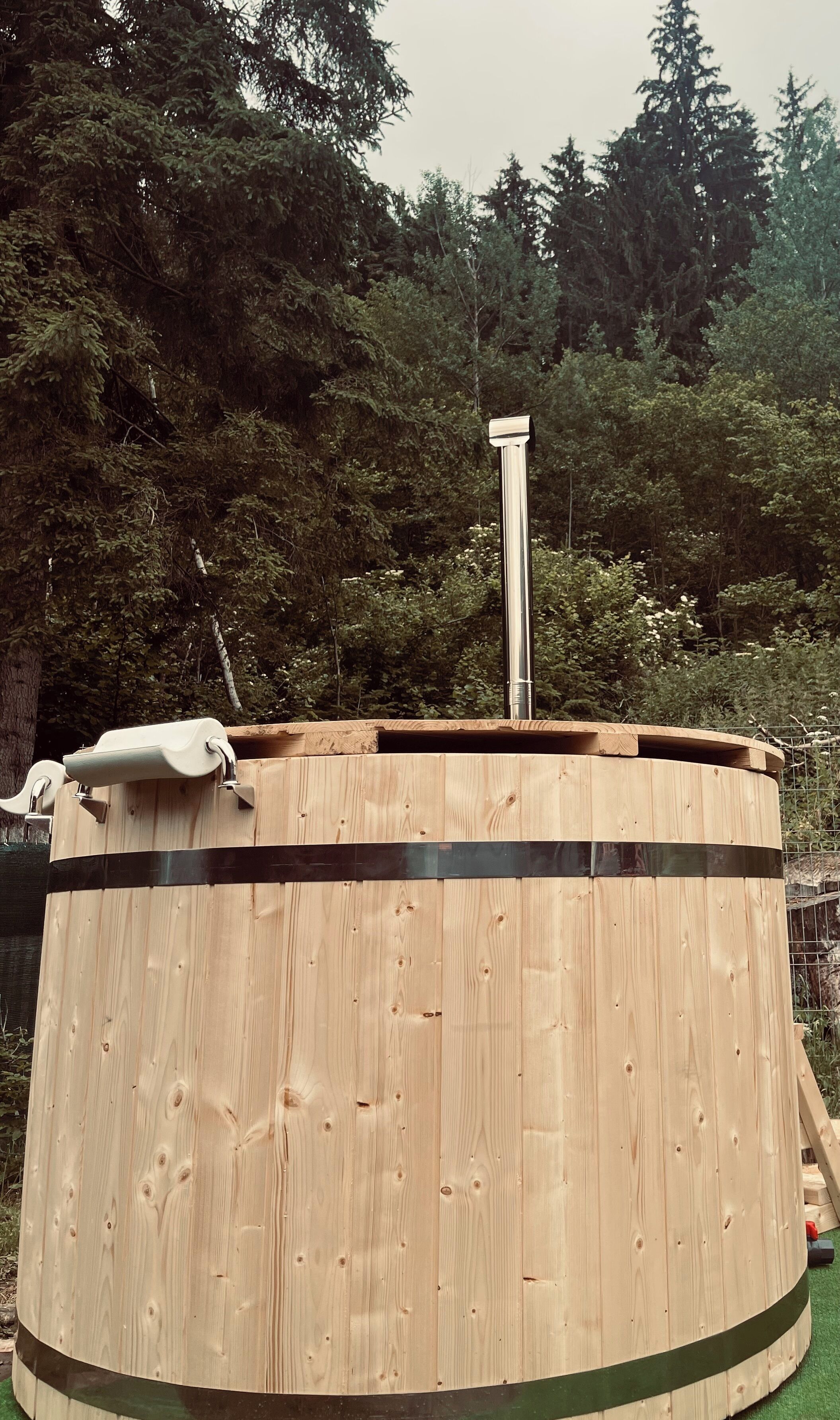 Uma sauna de madeira com um mastro metálico numa área arborizada.