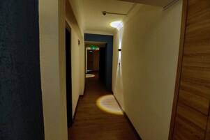 Um corredor estreito com piso de madeira, paredes brancas e uma parede azul de destaque.