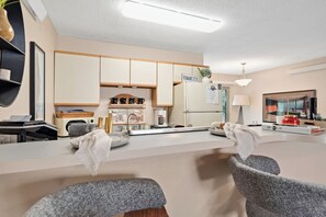 Uma cozinha moderna com uma ilha central, armários de madeira, uma geladeira e um espaço de refeições com cadeiras.