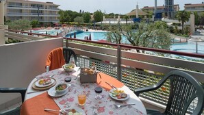 Uma varanda com uma mesa posta para dois, com vista para uma piscina e uma torre.