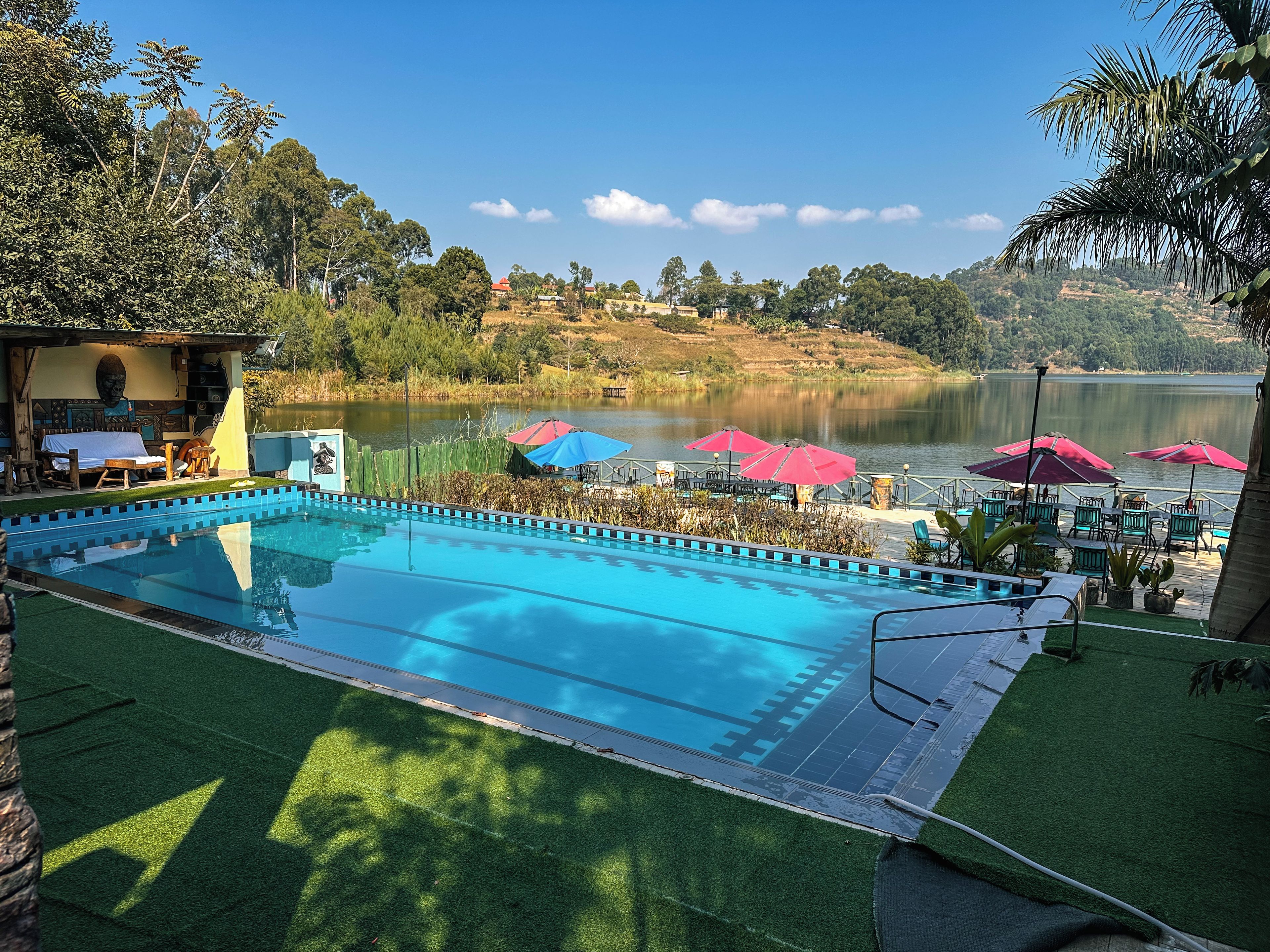 Piscina com vista para um lago e colinas, cercada por áreas de estar ao ar livre e guarda-sóis.