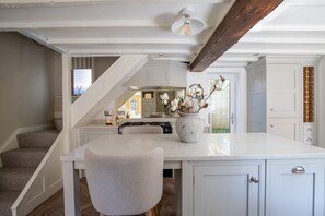 Cozinha com ilha central, armários brancos, escada de madeira e vista para o exterior.