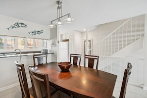 Uma sala de jantar com uma mesa e cadeiras de madeira, uma cozinha ao fundo e uma escada.