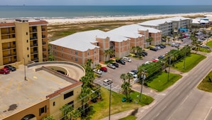 Um hotel com vários edifícios, estacionamento e uma praia ao fundo.