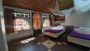 Quarto com duas camas, janela com cortinas estampadas, teto tecido e piso padronizado.
