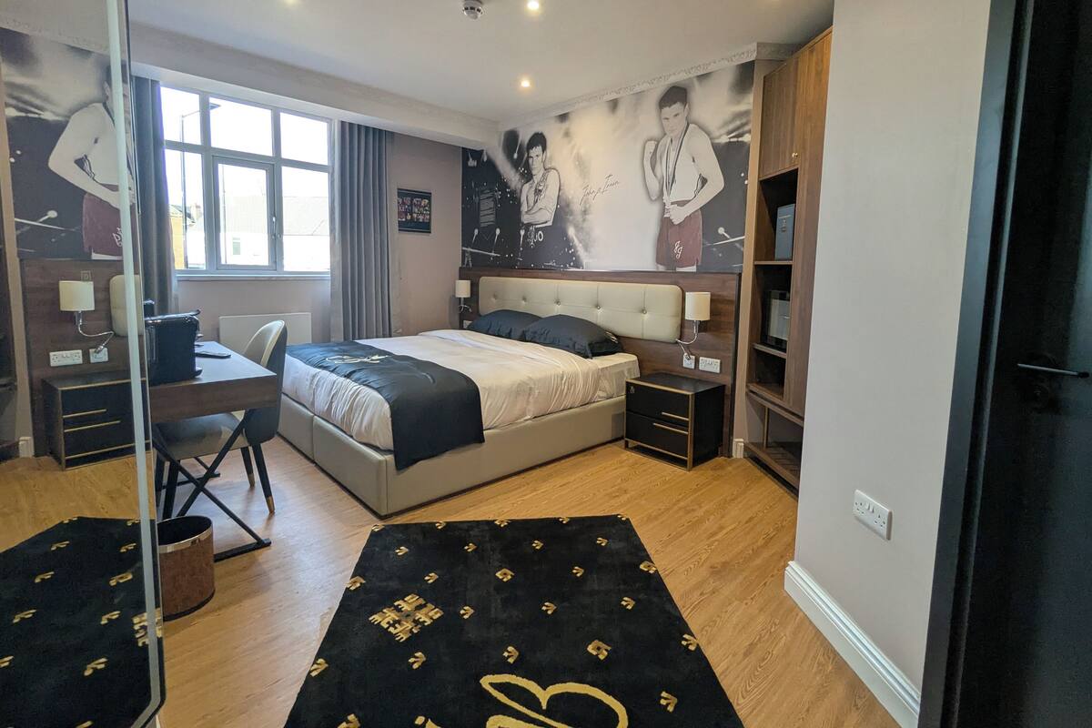 Quarto moderno com cama, escrivaninha e cadeira, uma janela grande e uma parede com um cartaz.