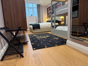 Um quarto com uma cama beliche, uma escrivaninha com cadeira, uma janela e um tapete.