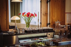 Disposição de buffet com diversos alimentos, um vaso de flores e um abajur.
