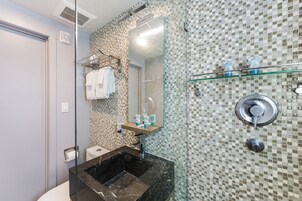 Casa de banho moderna com cabine de chuveiro em vidro, lavatório em mármore preto e parede com mosaico de azulejos.
