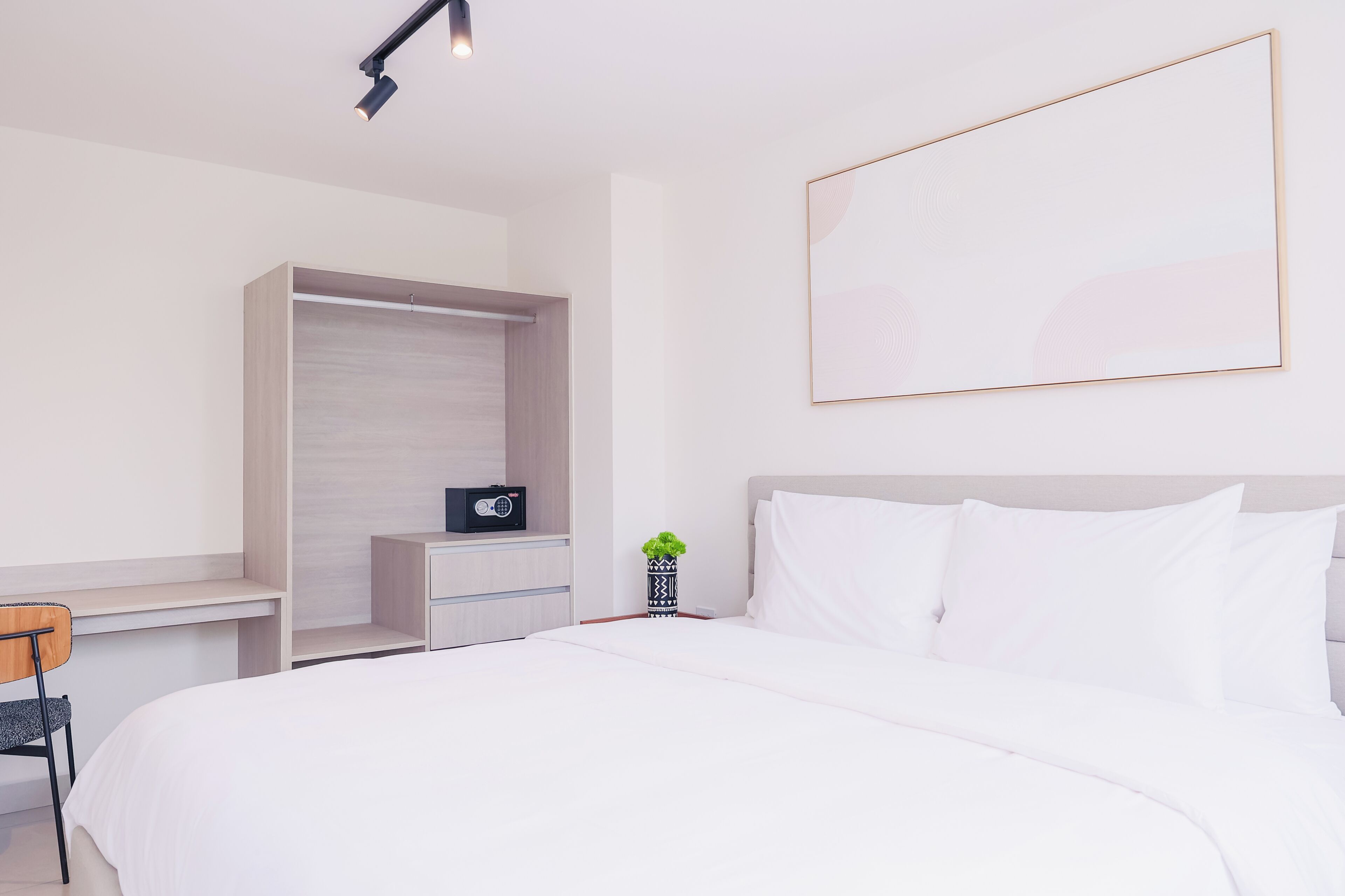Quarto de hotel moderno com uma cama grande, uma escrivaninha, um guarda-roupa e uma mesa de cabeceira com um rádio e uma planta.