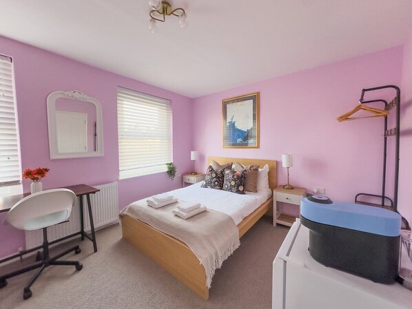 Quarto com cama, mesa de cabeceira, luminária, cadeira, escrivaninha e radiador.