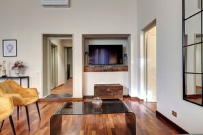 Uma sala de estar moderna com uma TV de tela plana presa a uma estante de madeira, uma mesa de centro de vidro e uma poltrona amarela.