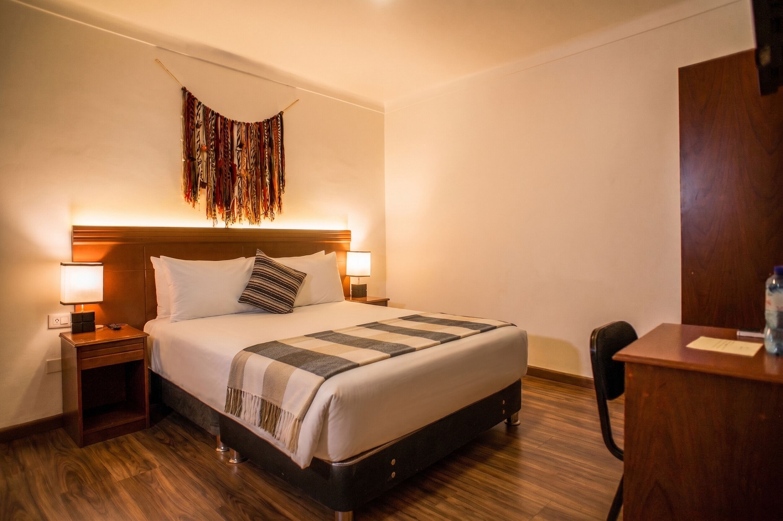 Quarto de hotel com cama, abajures, escrivaninha e uma cadeira.