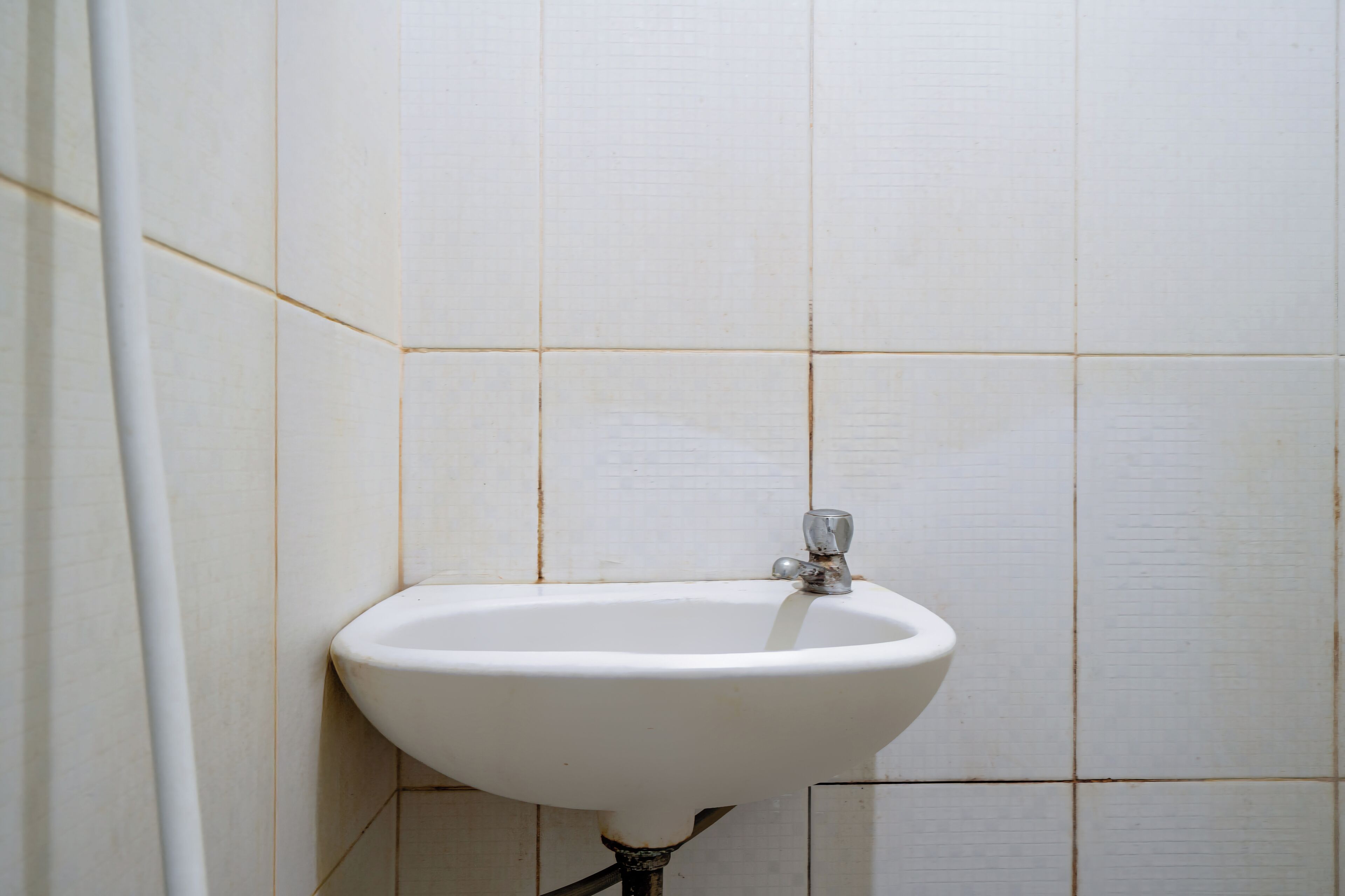 Uma pia branca assentada sobre pedestal com uma torneira simples num banheiro com paredes revestidas de azulejos brancos.