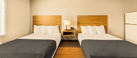 Quarto de hotel com duas camas, uma mesa de cabeceira com abajur e cabeceira de madeira.