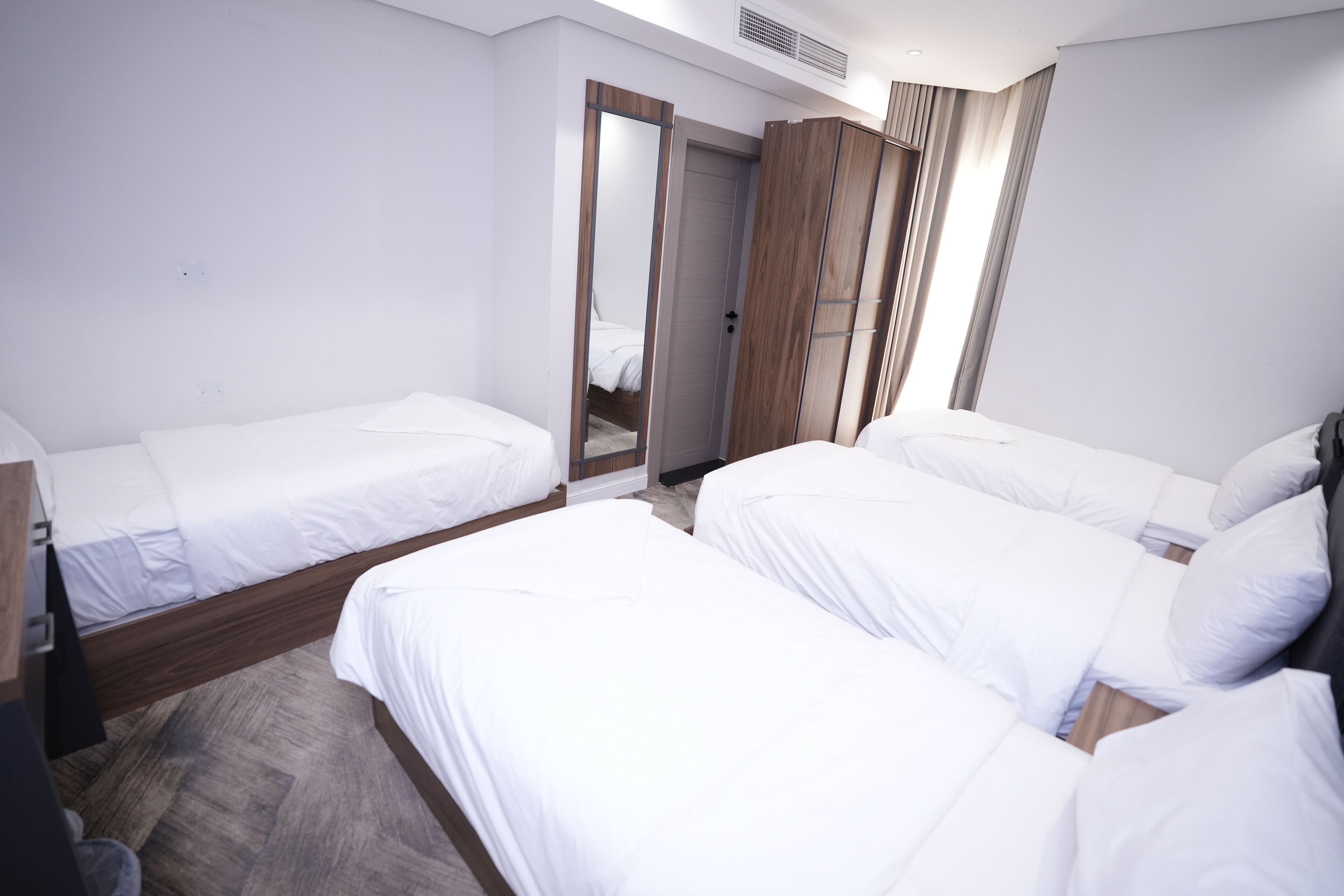 Quarto de hotel com duas camas de solteiro, um guarda-roupa de madeira e um espelho.