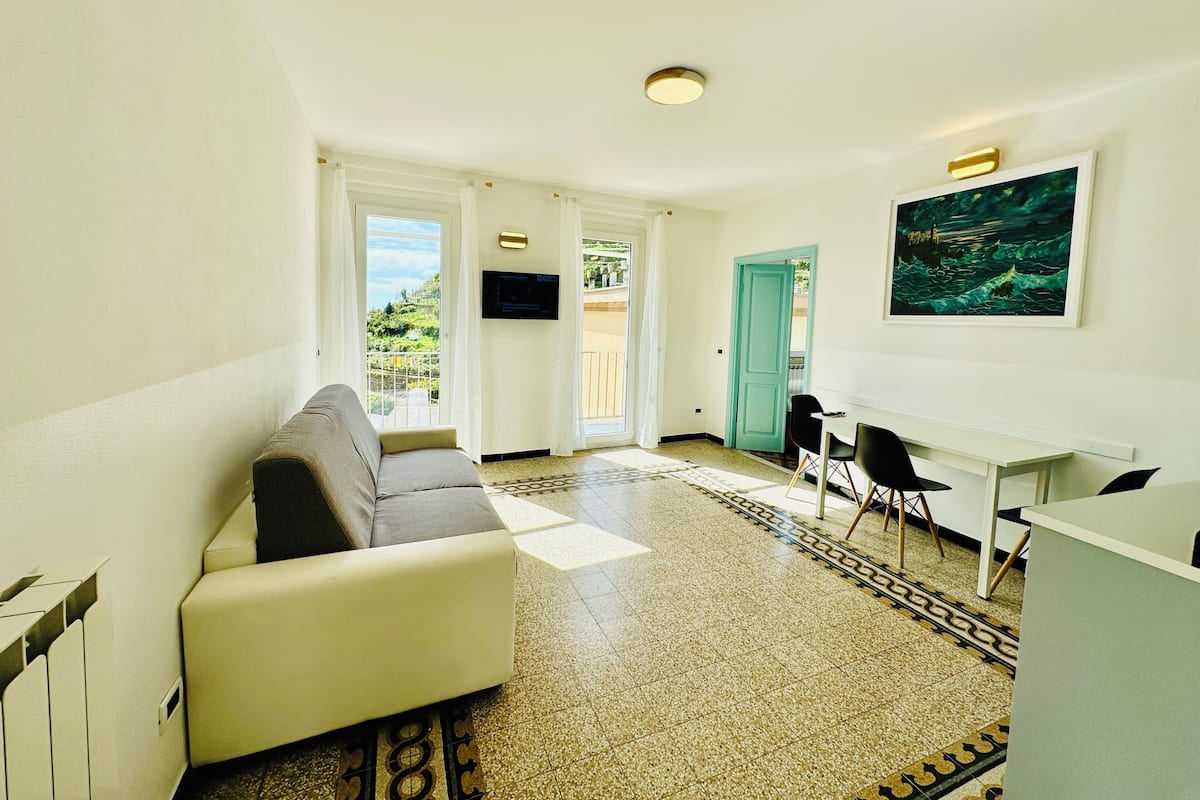 Uma sala de estar com sofá, televisão, escrivaninha e cadeiras.