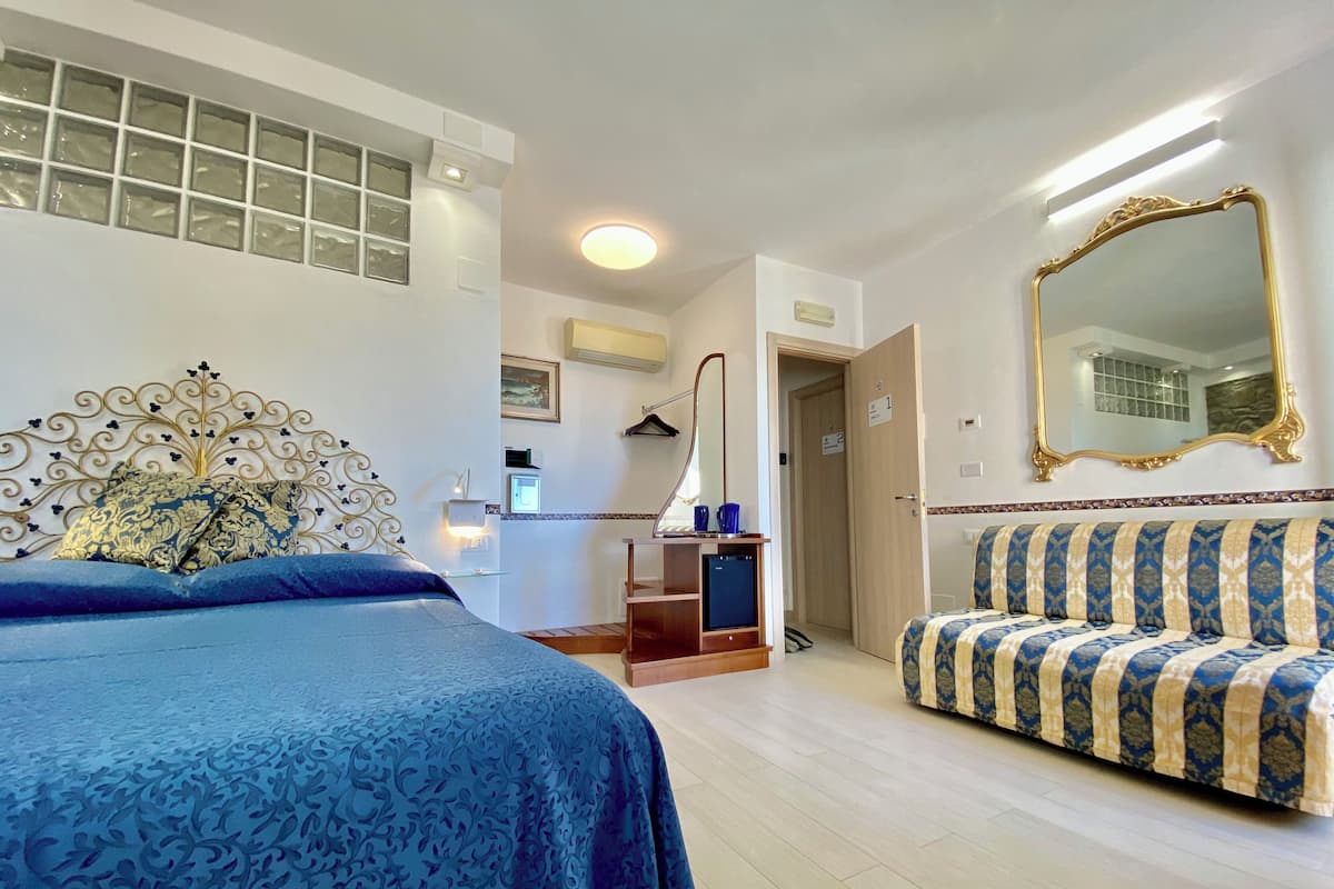 Quarto de hotel com cama, sofá, espelho e porta que dá para outro aposento.
