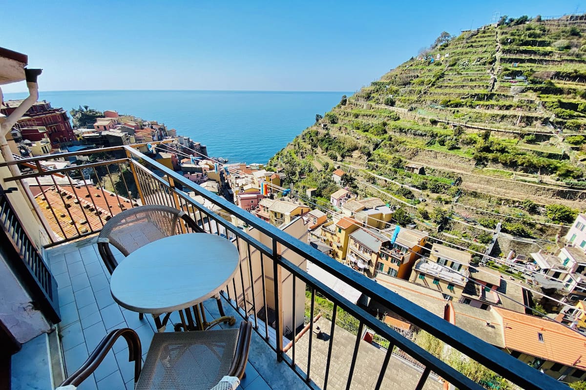 Varanda com mesa e cadeiras com vista para uma vila costeira e o mar.