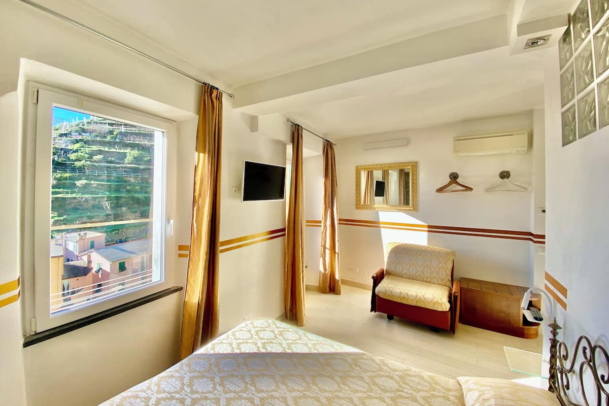 Quarto de hotel com cama, poltrona, televisão e janela com cortinas.