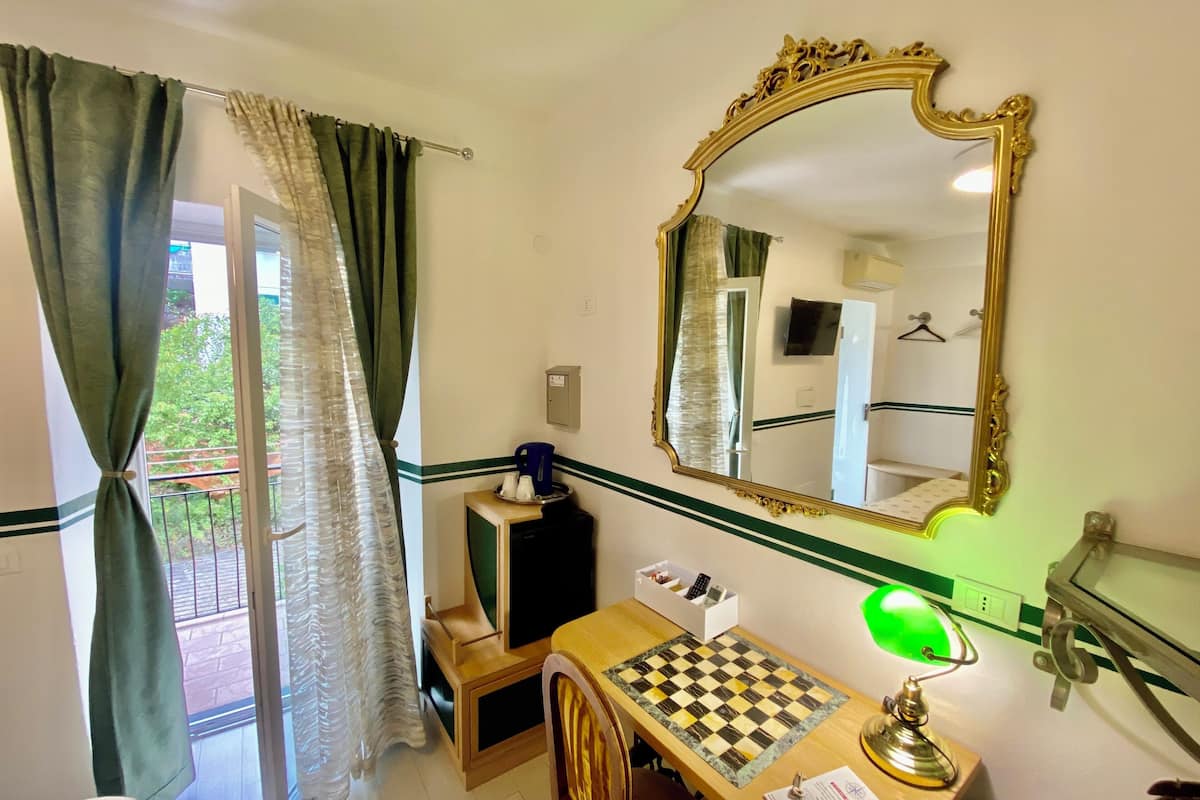 Quarto com escrivaninha, espelho, um tabuleiro de xadrez, abajur e vista para o exterior através de uma janela com cortinas.