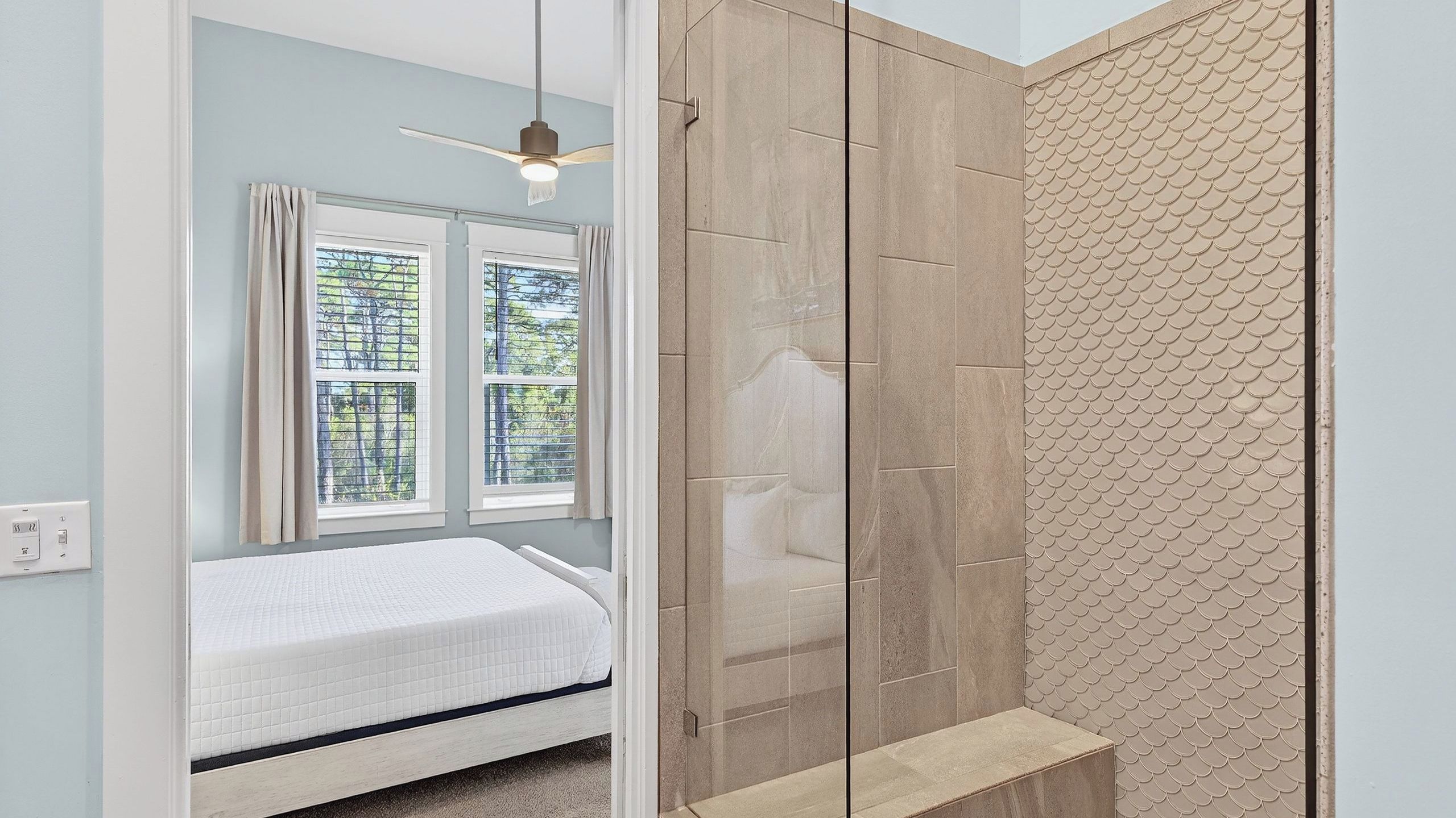 Quarto com cama, ventilador de teto, janela com cortinas e parede com padrão de escamas de peixe.