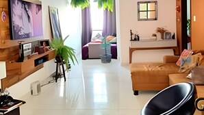 Uma sala de estar moderna com um sofá, uma cadeira preta, uma televisão e uma luminária no teto.
