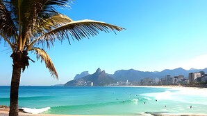 Uma praia com águas turquesa cristalinas, palmeiras e montanhas ao fundo.