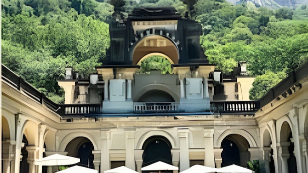 Área da piscina com vista para uma montanha e um edifício com arcos e guarda-sóis.