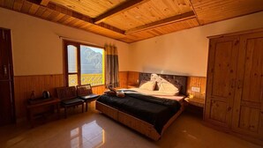 Quarto com teto de madeira, uma cama, um banco, janela com cortinas e um guarda-roupa.