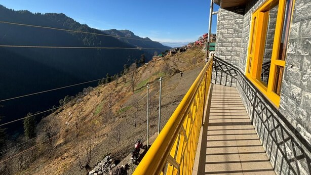 Um edifício de pedra com janelas amarelas e uma varanda com vista para uma paisagem montanhosa e um corpo de água.