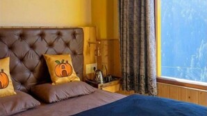 Quarto com cabeceira estofada, cama com colcha azul, duas almofadas com padrão de abóbora, mesa de cabeceira com luminária e janela com cortinas.