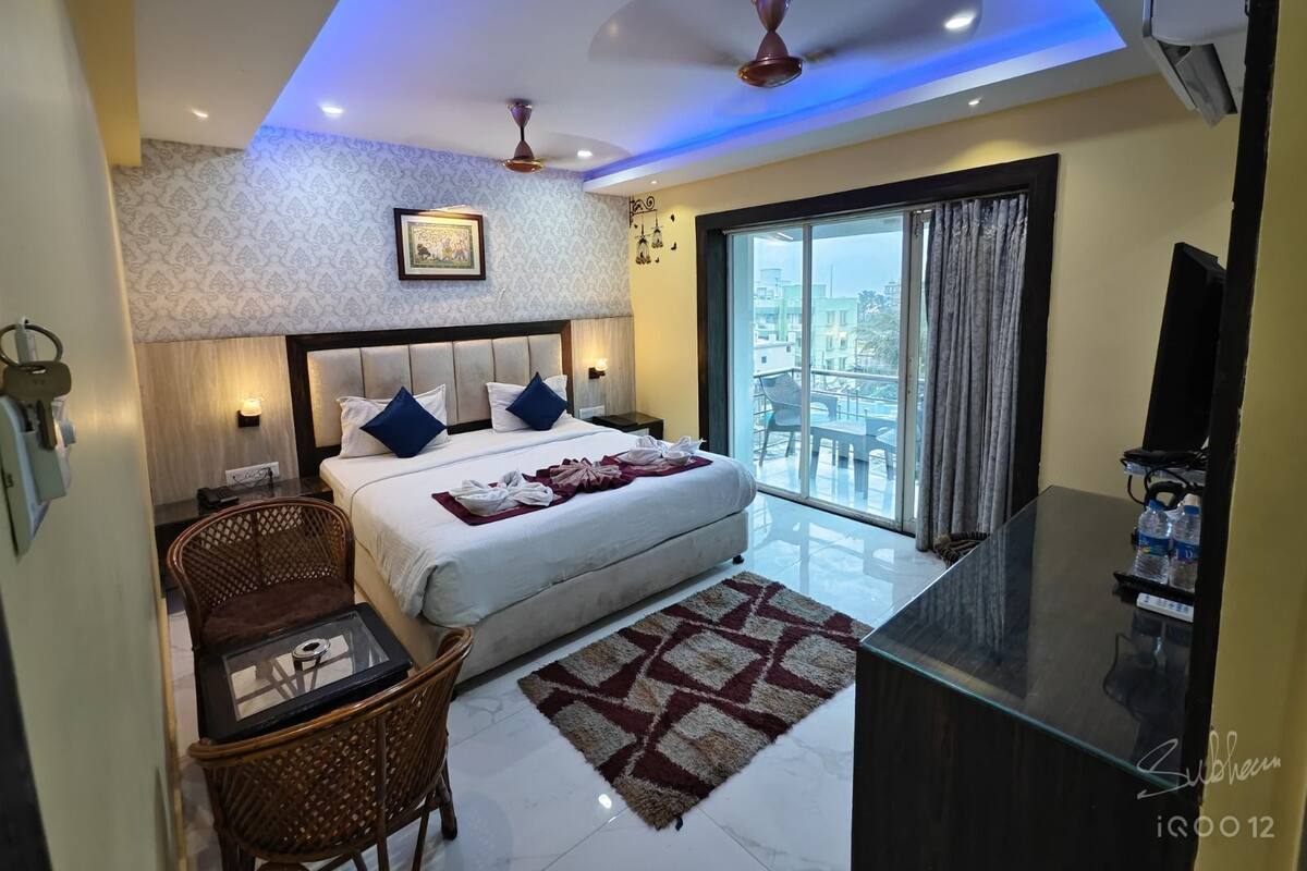 Quarto de hotel moderno com uma cama grande, uma mesa com cadeira, uma varanda com vista e um ventilador de teto.