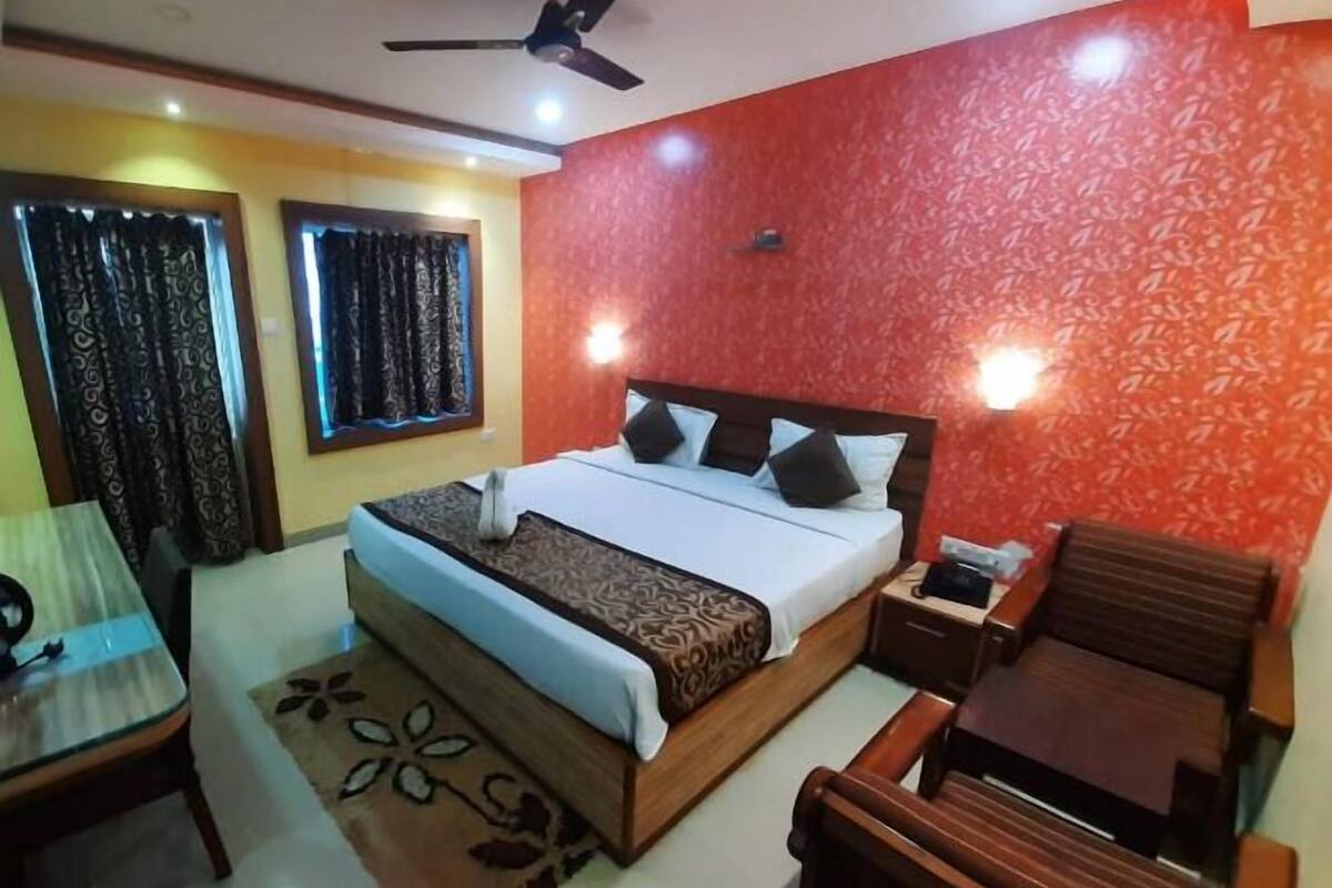 Quarto de hotel com cama, escrivaninha, cadeira, ventoinha no teto e parede com padrão vermelho.