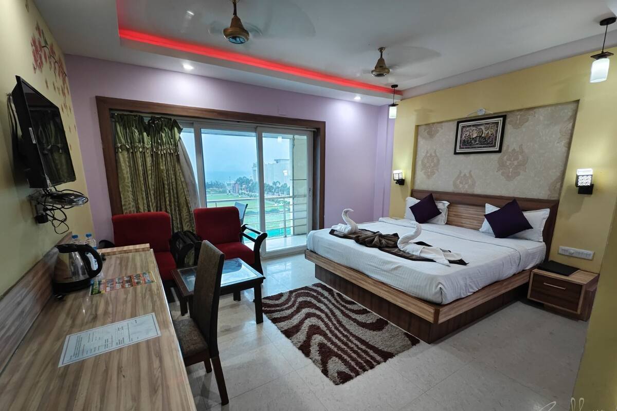 Quarto de hotel com cama, secretária, cadeiras, vista da cidade e uma janela grande.