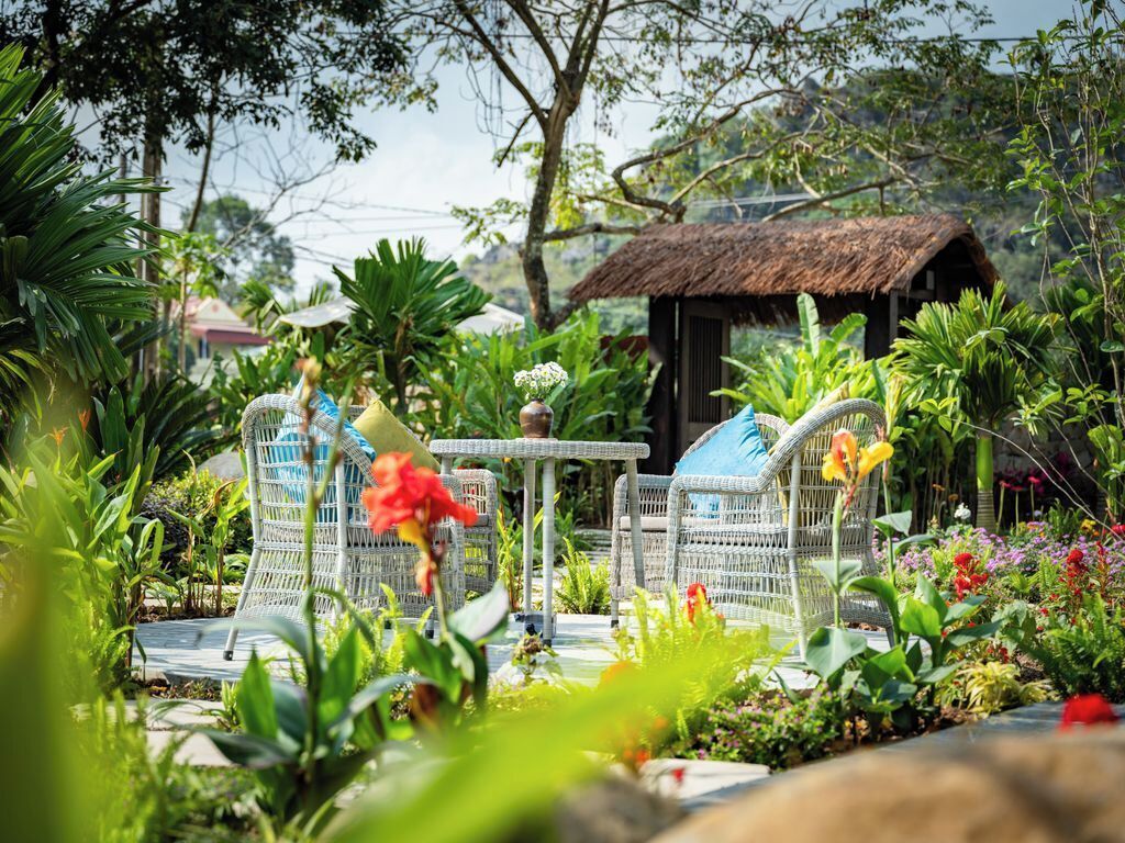 Um jardim com cadeiras de vime, uma mesa pequena e uma estrutura com telhado de palha.